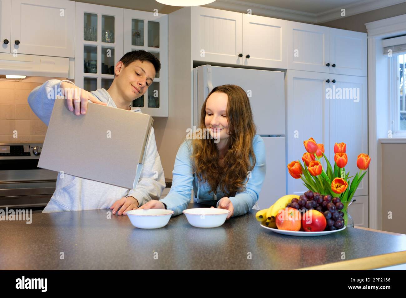 Smiling, happy boy and girl pouring frosted chocolate balls out of the ...