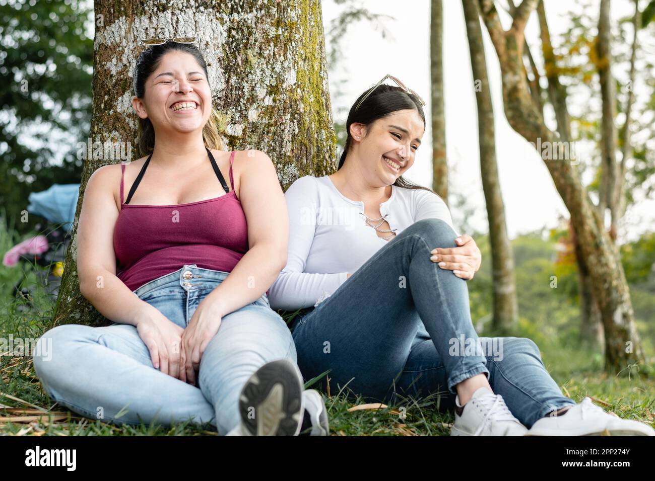 young women sitting on the ground next to a tree, talking and laughing ...