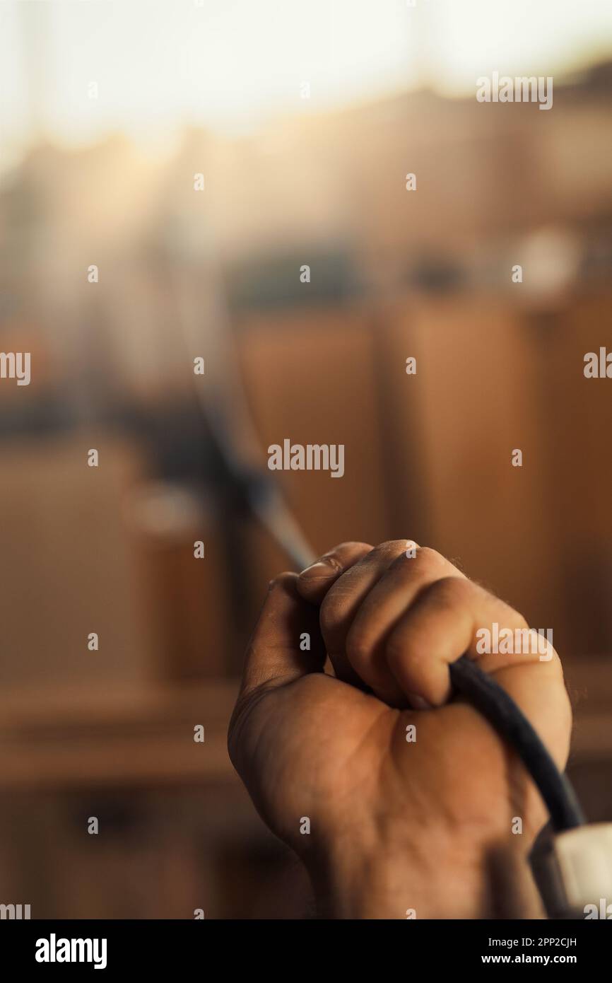 A strong male hand is in focus as it grips and pulls a thick electrical ...