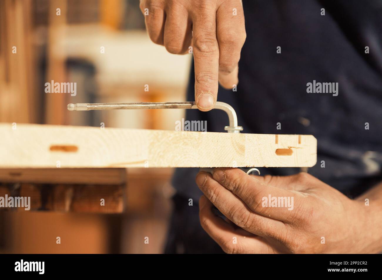 The carpenter screws and secures a wooden board using an Allen key ...