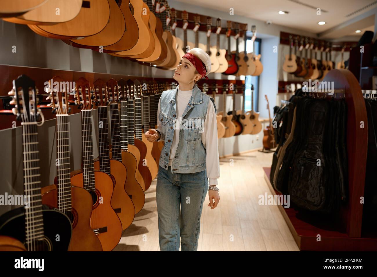 Young hipster woman buyer choosing acoustic guitar in instrument shop ...
