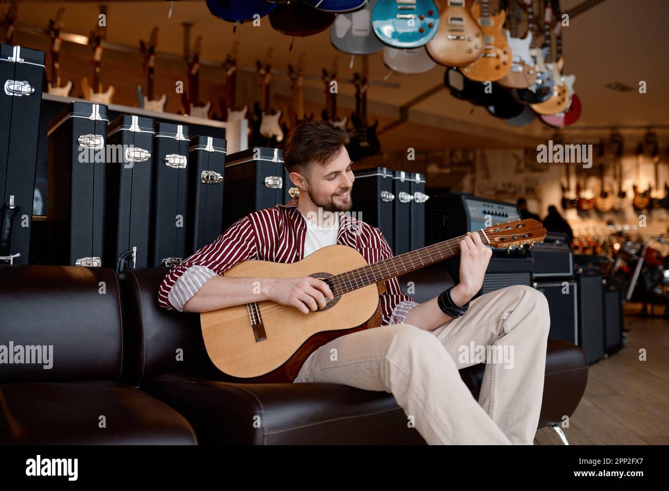Happy man musician playing guitar over string instrument shop store ...