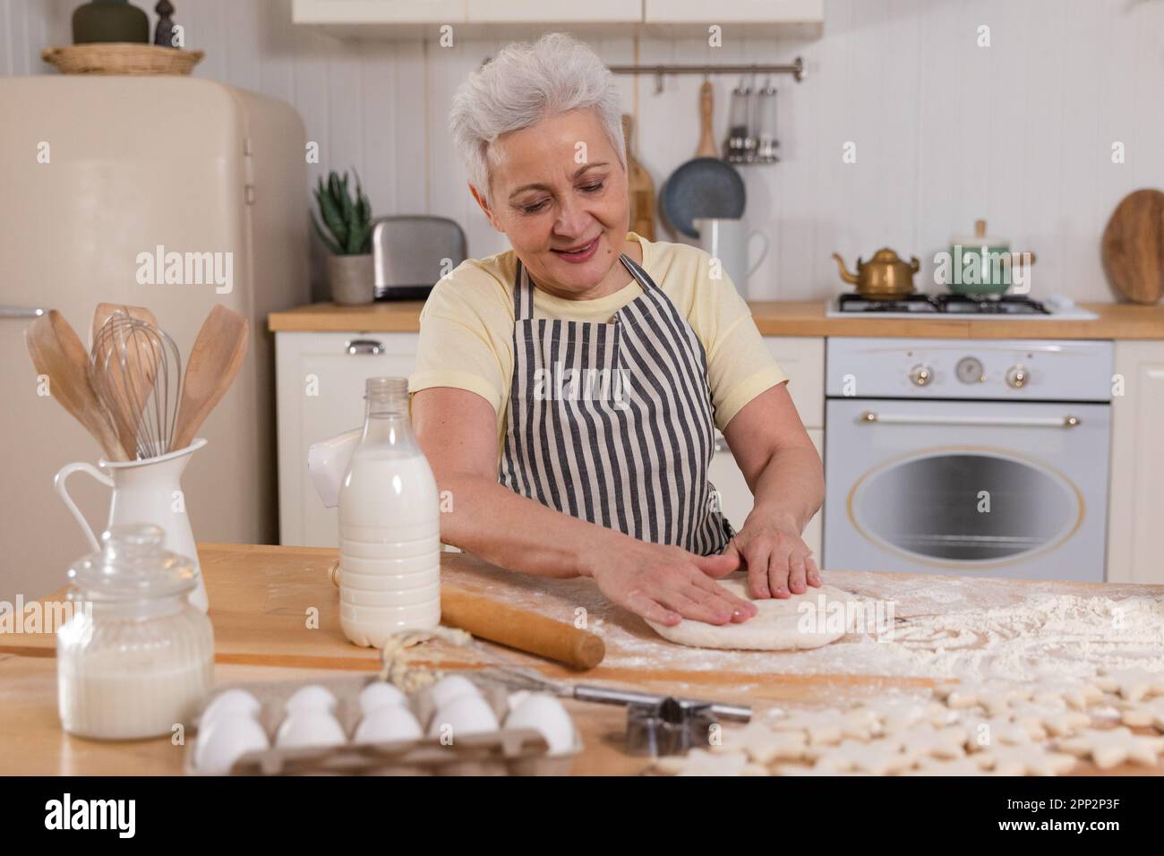 Happy senior woman cooking in kitchen. Stylish older mature gray haired ...