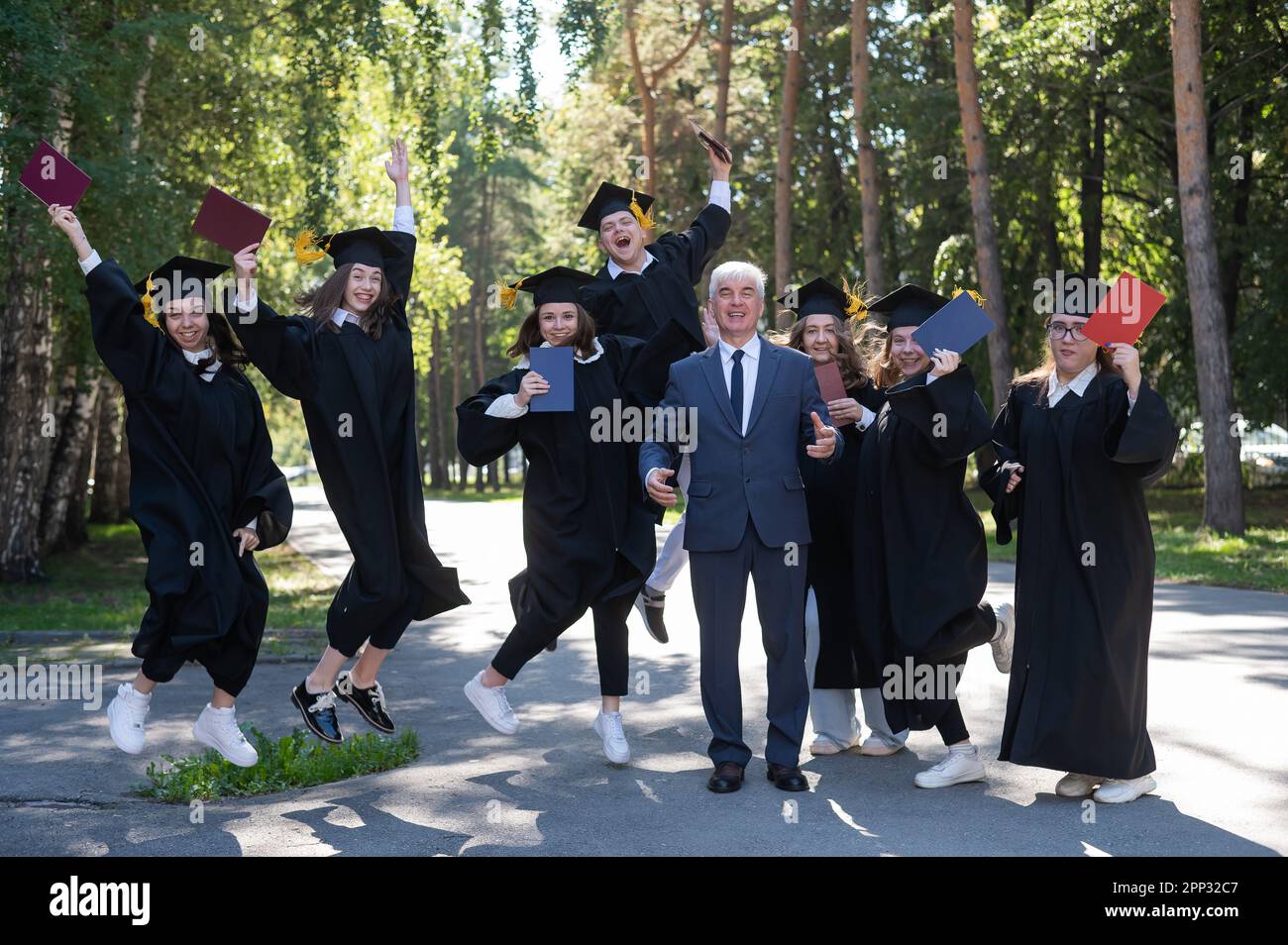 A university professor and seven robed graduates are jumping outdoors ...