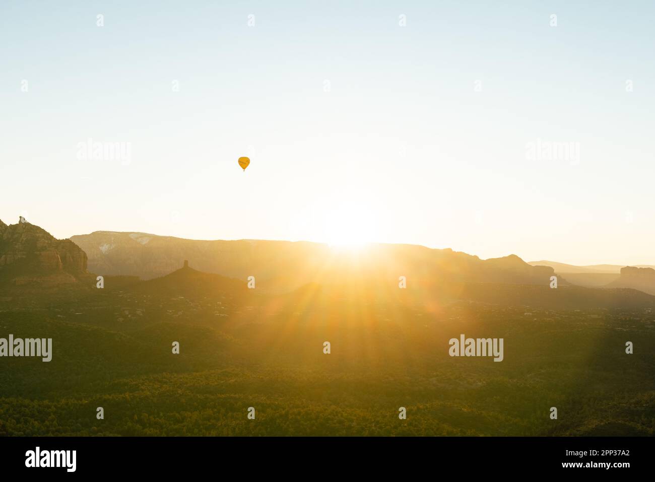 Wide shot of single hot air balloon in sky as sun rises above red rock ...