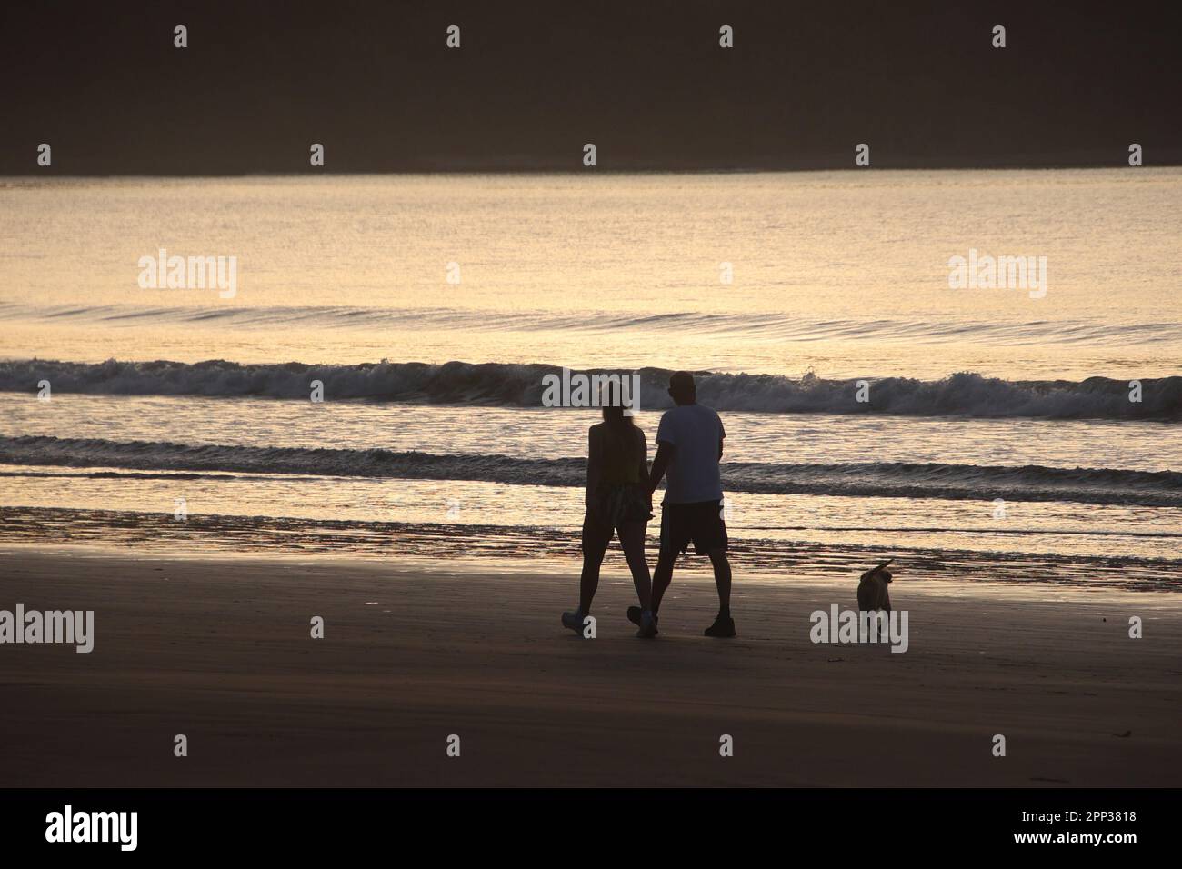 As the sun peeks over the horizon, a two people stroll along the beach ...