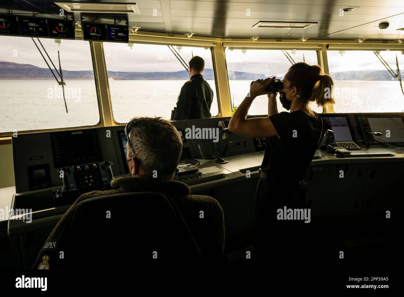 Officer looks through binoculars from the bridge of the patrol ship ...