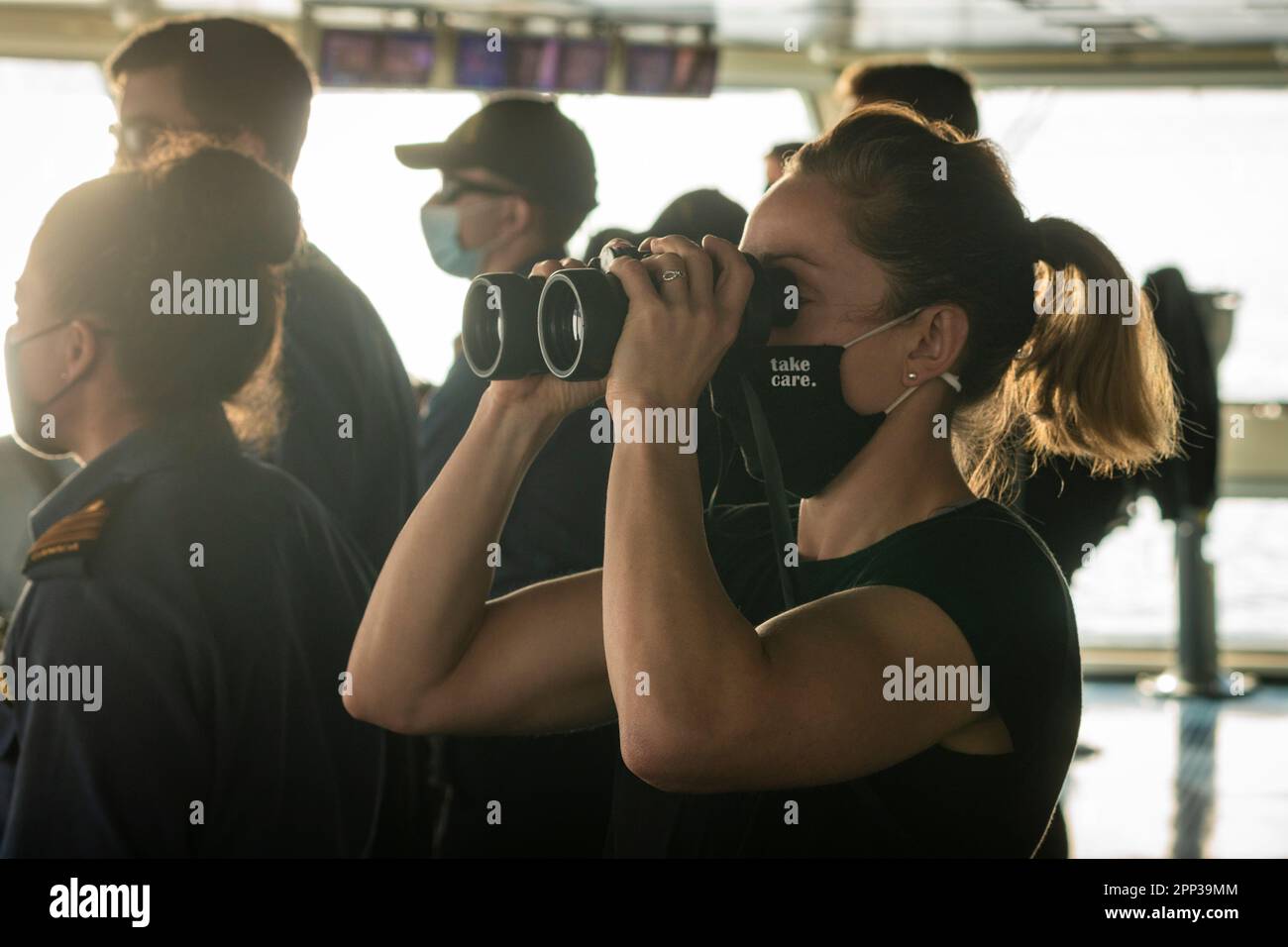 Officer looks through binoculars from the bridge of the patrol ship ...