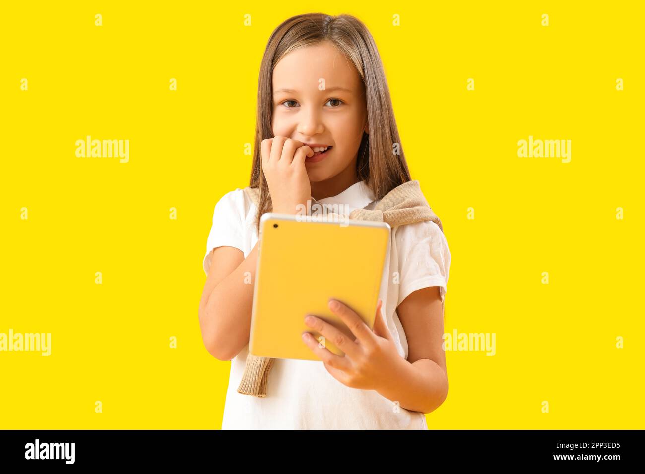 Little girl with tablet computer biting nails on yellow background ...