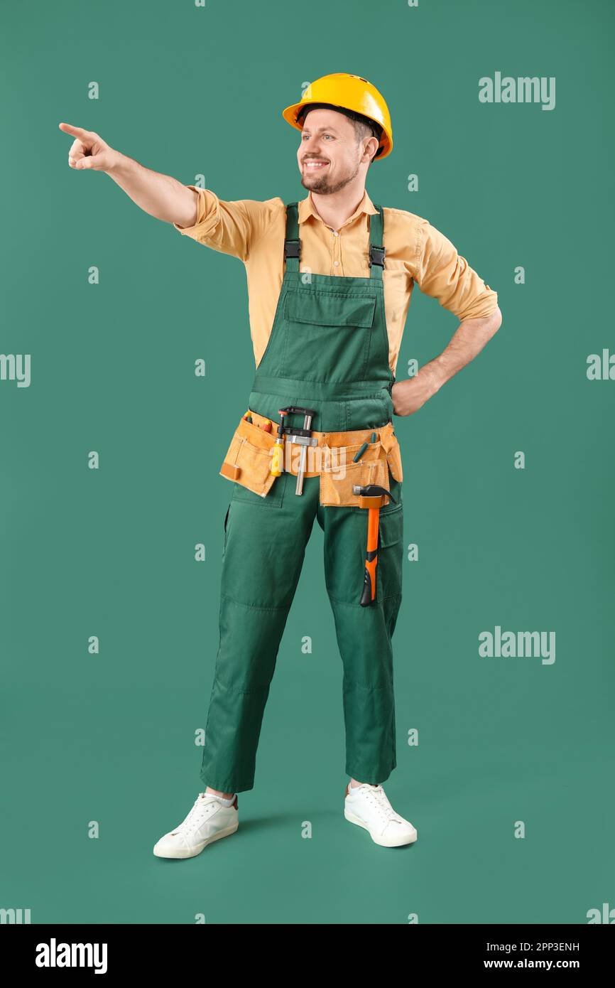 Male carpenter in hardhat pointing at something on green background ...
