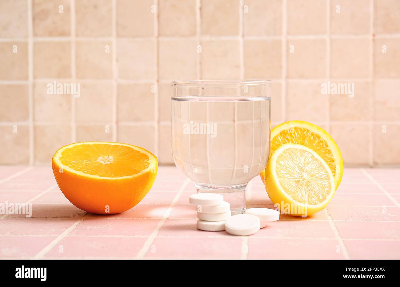 Glass of water, vitamin C effervescent tablets and fruits on pink tiled ...