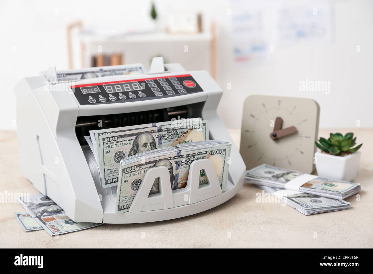 Modern cash counting machine with dollar banknotes and clock on table ...