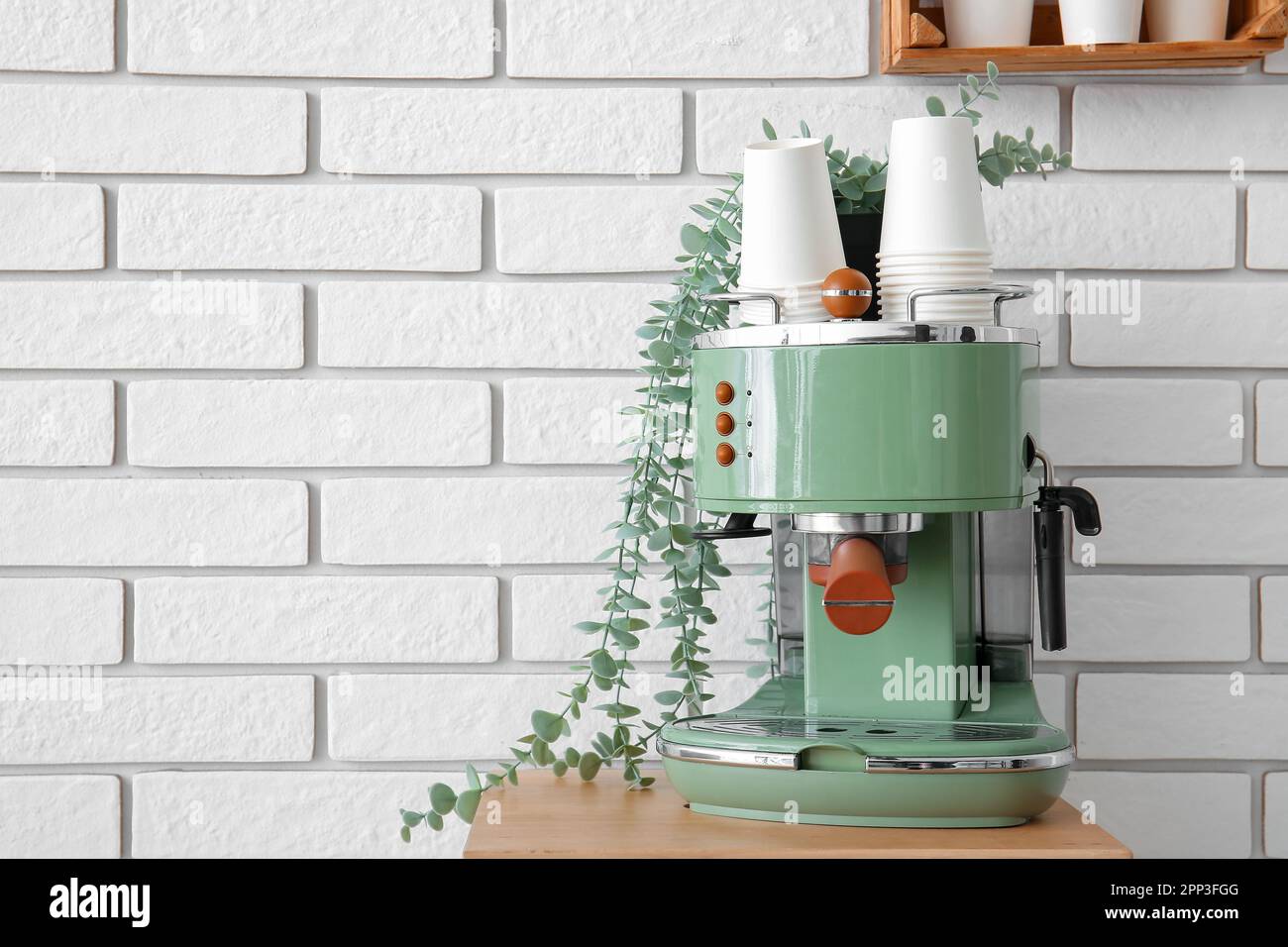 Modern coffee machine with paper cups and houseplant on table near white brick wall Stock Photo ...