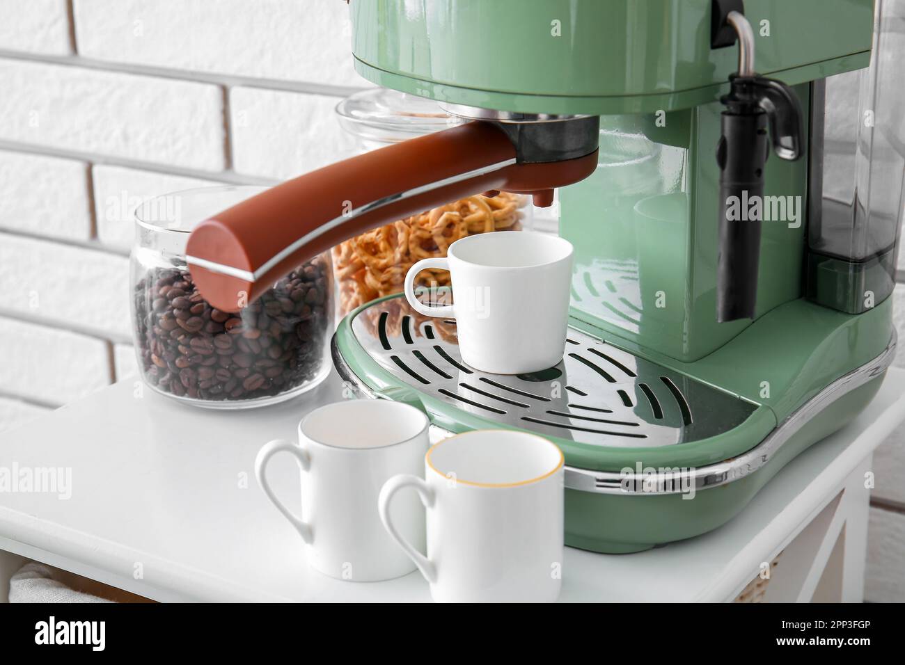 Modern coffee machine with cups, snacks and beans on table near white ...