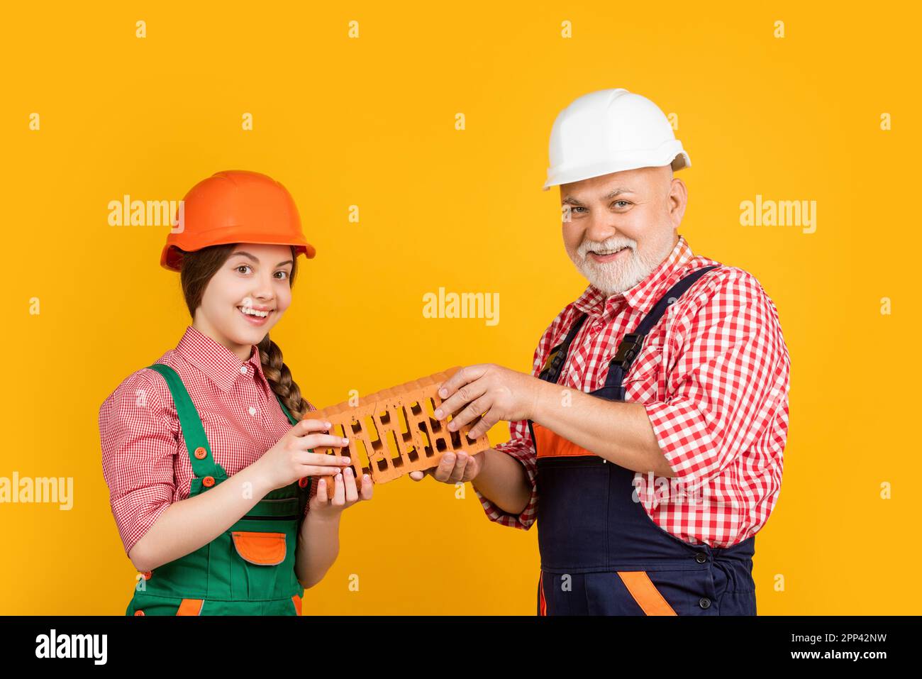 happy teen child and grandfather bricklayer in helmet on yellow ...