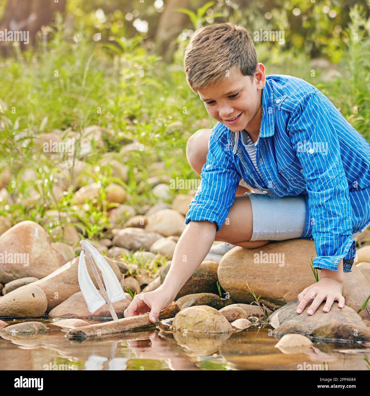 Setting her to sail. a young boy playing with a toy boat by the water ...