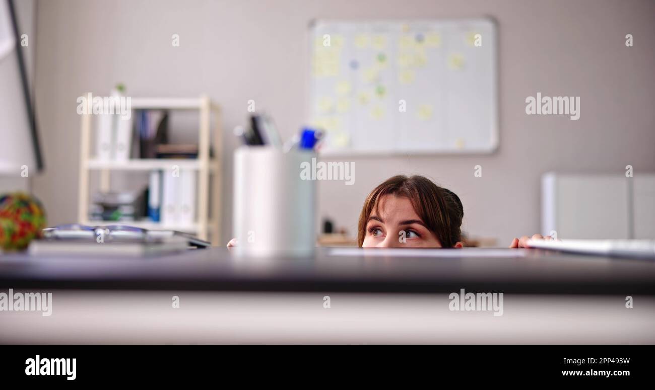 Scared Woman Hiding Behind Chair And Under Desk Stock Photo - Alamy