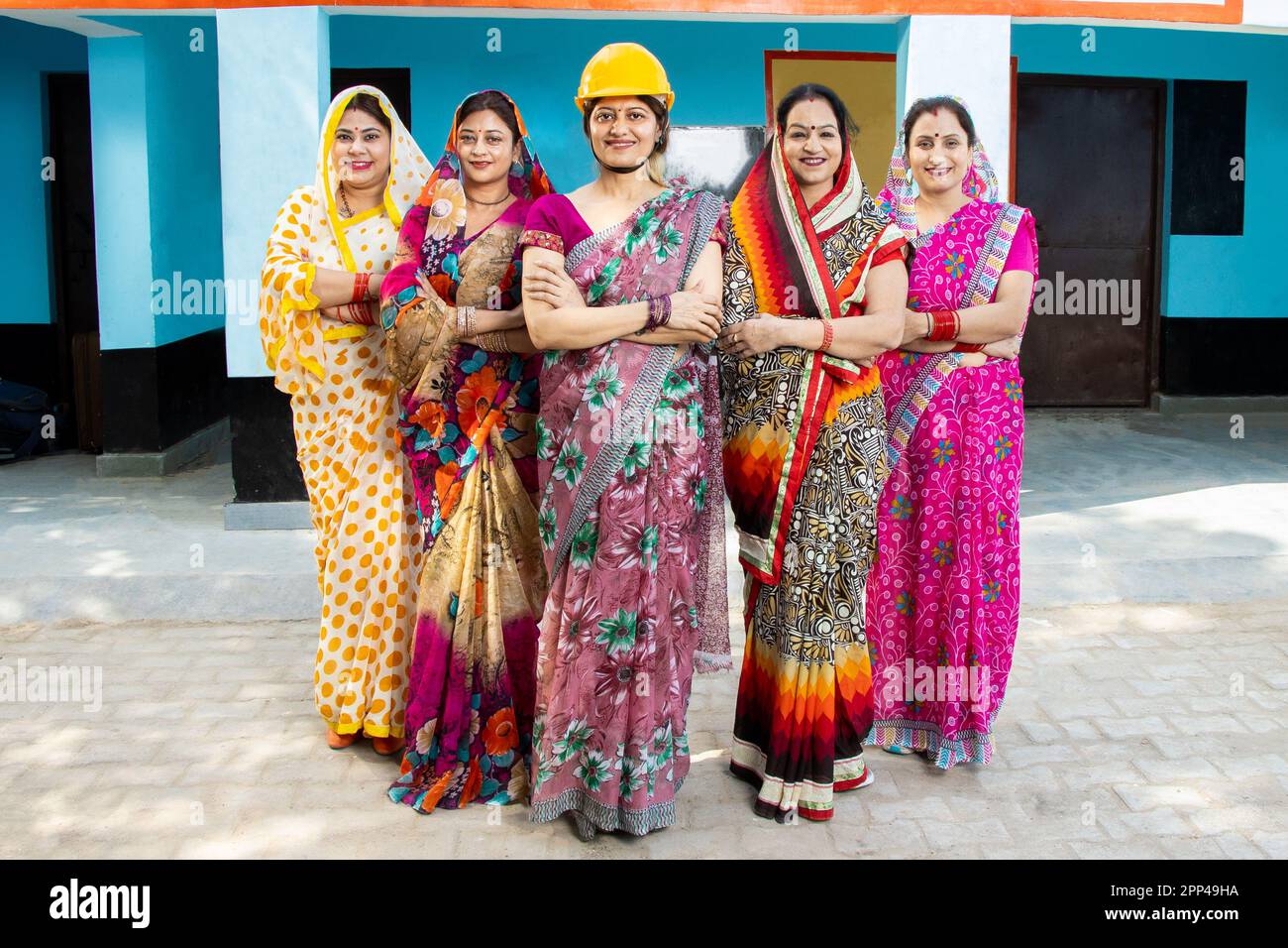 Group of confident young indian women wearing sari standing with female engineer wearing yellow ...