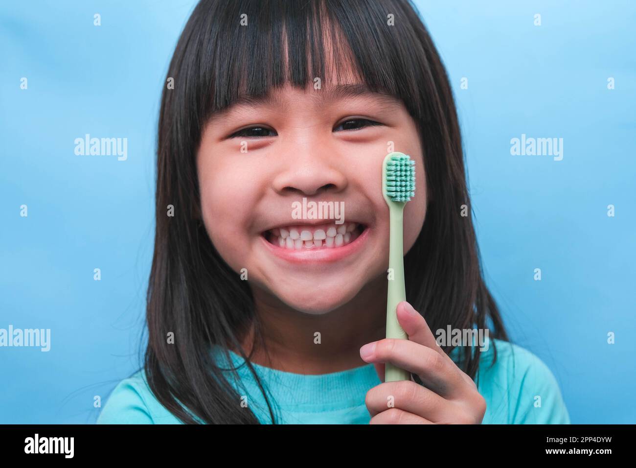 Smiling cute little girl holding toothbrush isolated on blue background ...