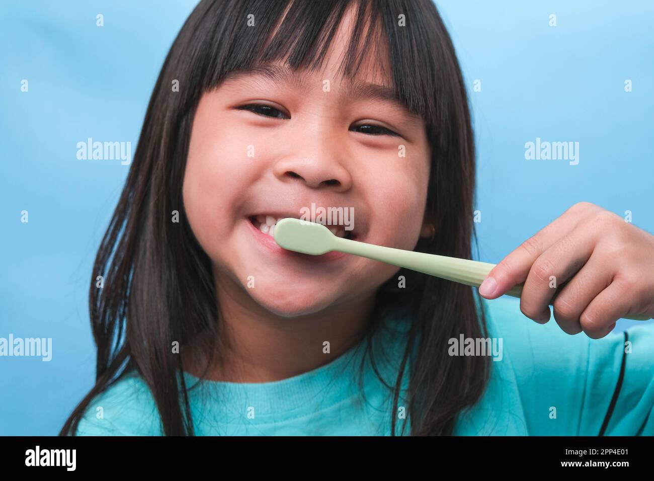 Smiling cute little girl holding toothbrush isolated on blue background ...