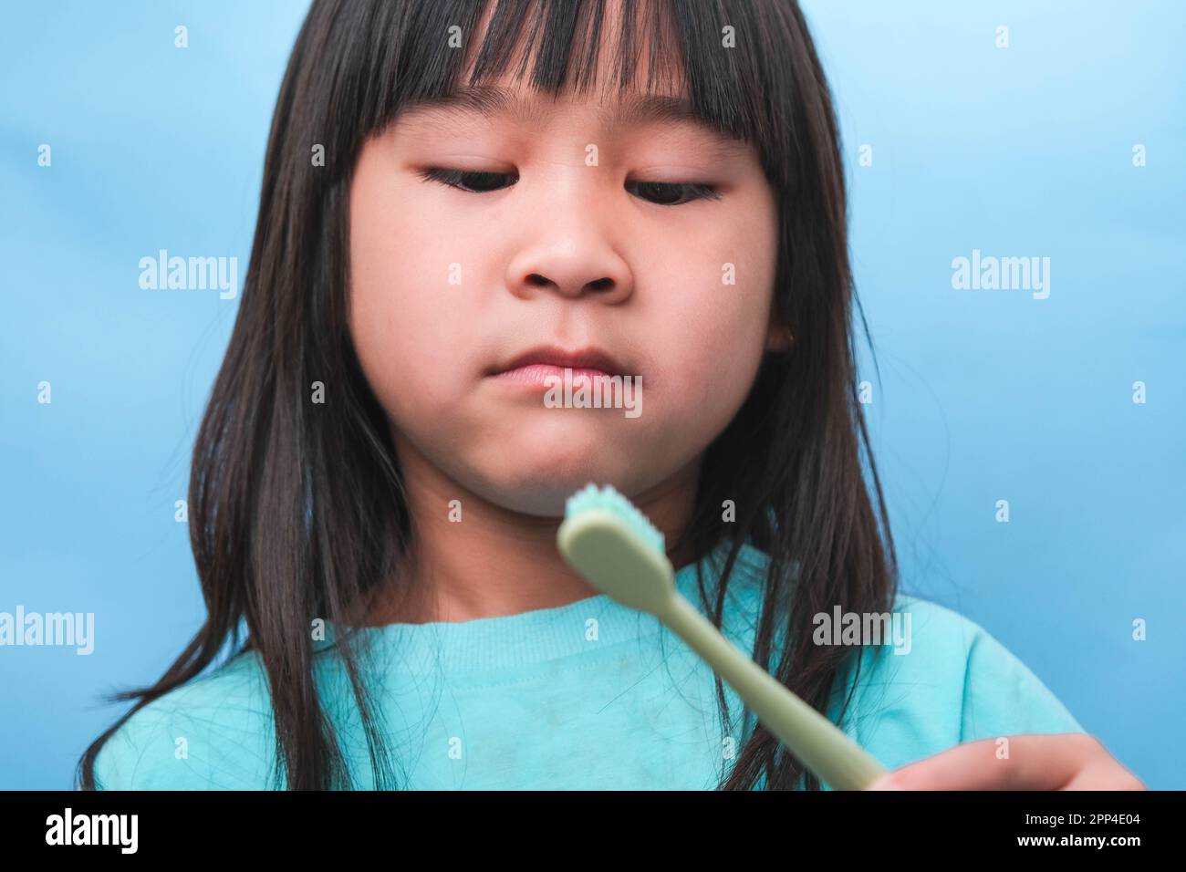 Smiling cute little girl holding toothbrush isolated on blue background ...