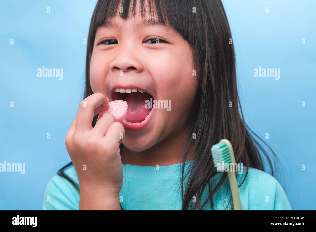 Smiling cute little girl holding toothbrush and sweets isolated on blue ...