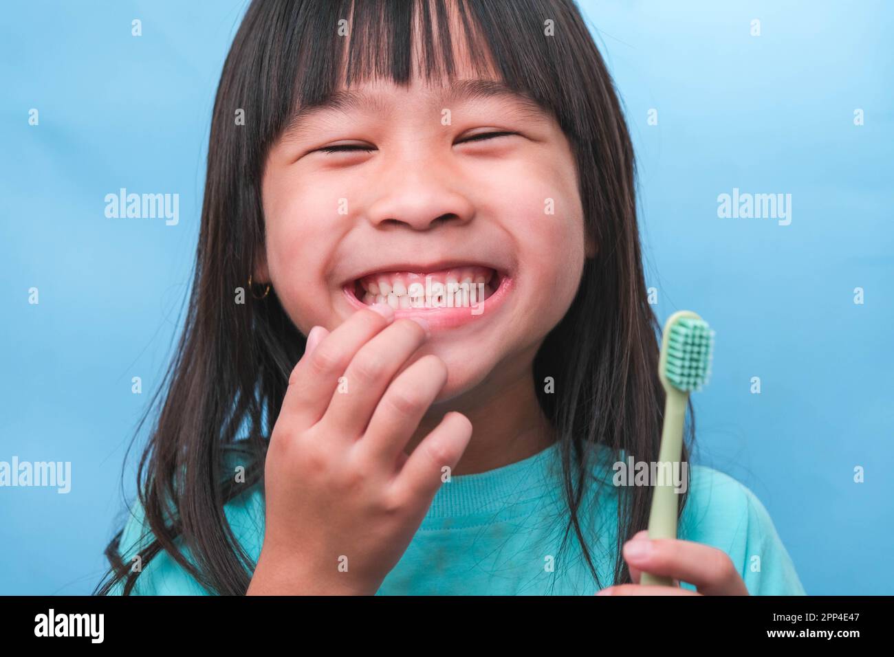 Smiling cute little girl holding toothbrush isolated on blue background ...
