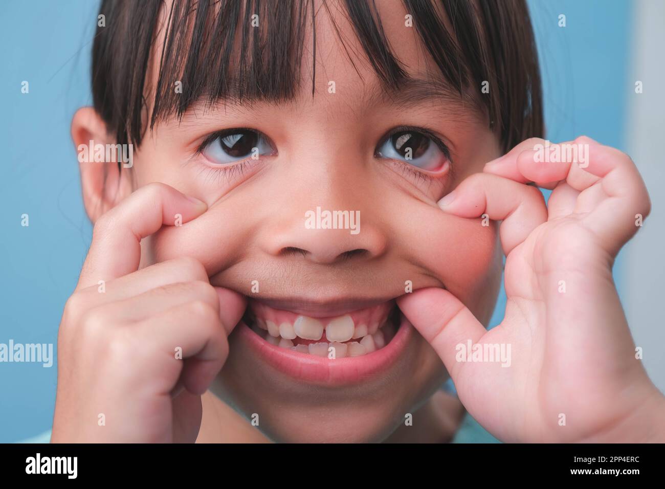 Cute little girl making a funny face with her hands on a blue ...