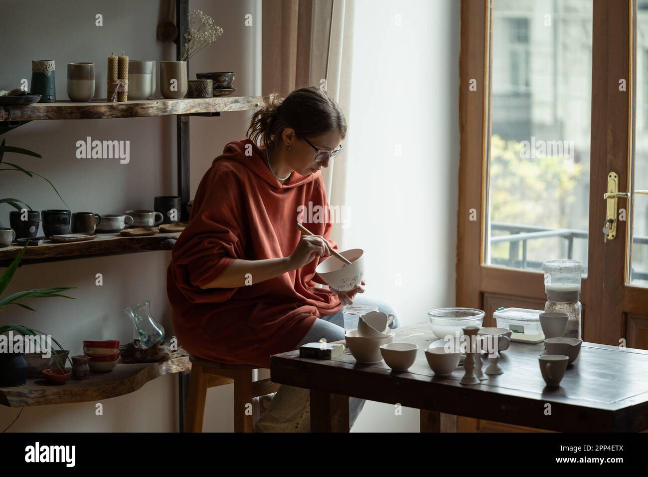 Focused artist woman creating ceramic pottery bowl use paintbrush sits ...