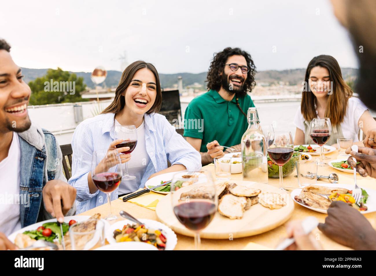 Smiling group of diverse friends having dinner at rooftop summer party ...