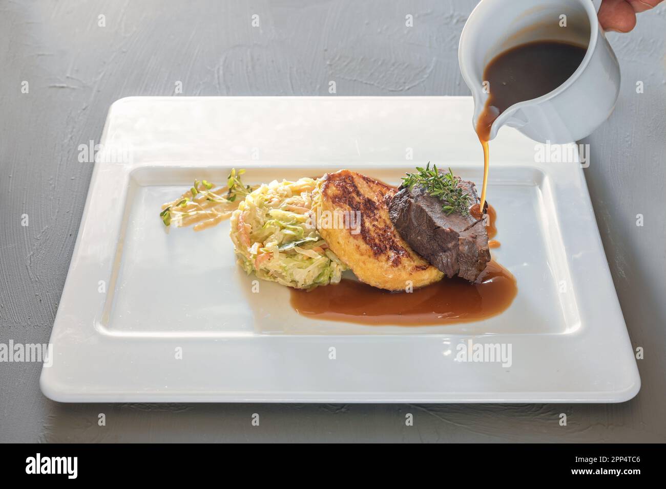 Pouring sauce on a dish from roast venison, flat bread dumpling and ...