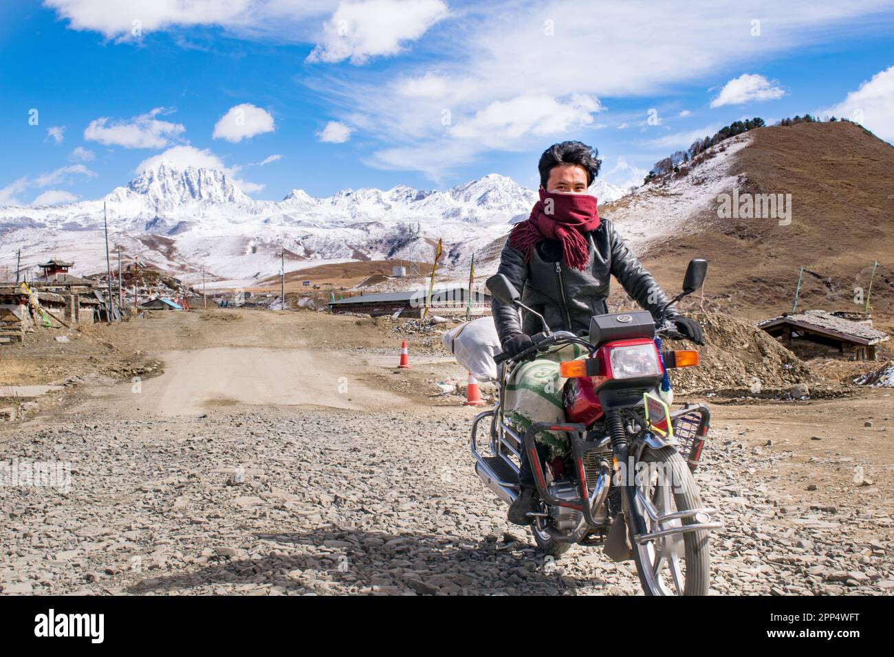 Tibetan man riding a motorcycle near Tagong town, in the background the ...