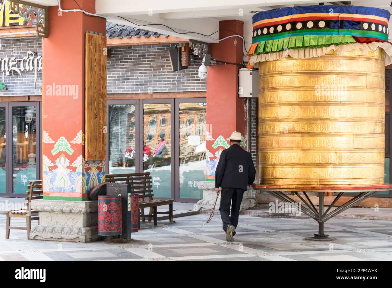 An elderly Tibetan man spins a human-sized Tibetan prayer wheel ...
