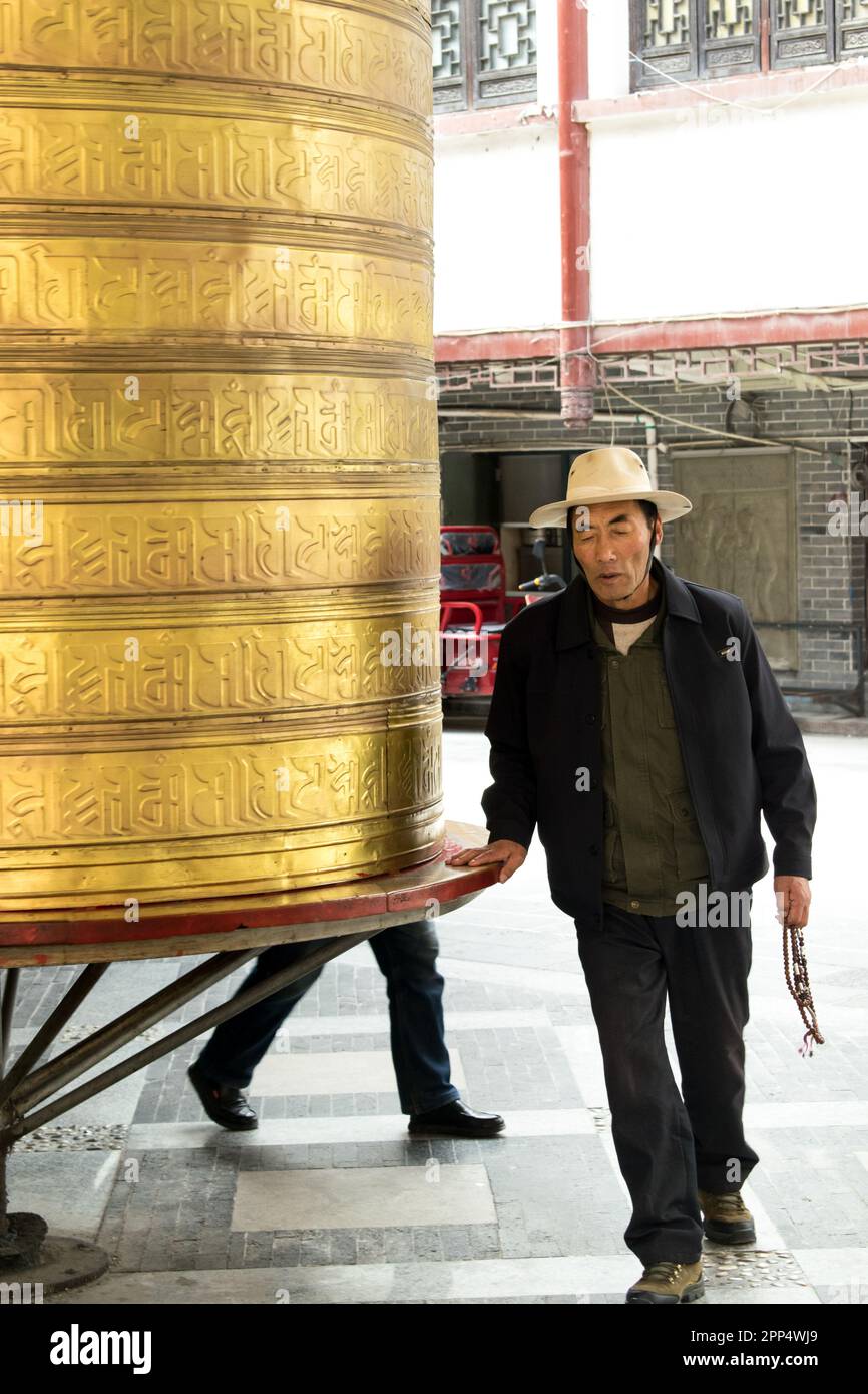An elderly Tibetan man spins a human-sized Tibetan prayer wheel ...