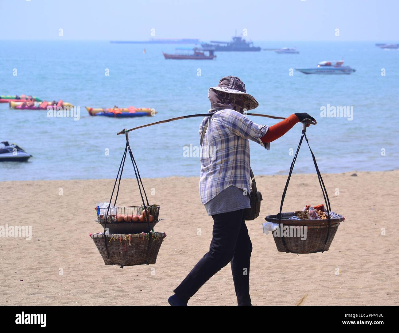 A person carries food for sale in two baskets suspended from a pole on ...
