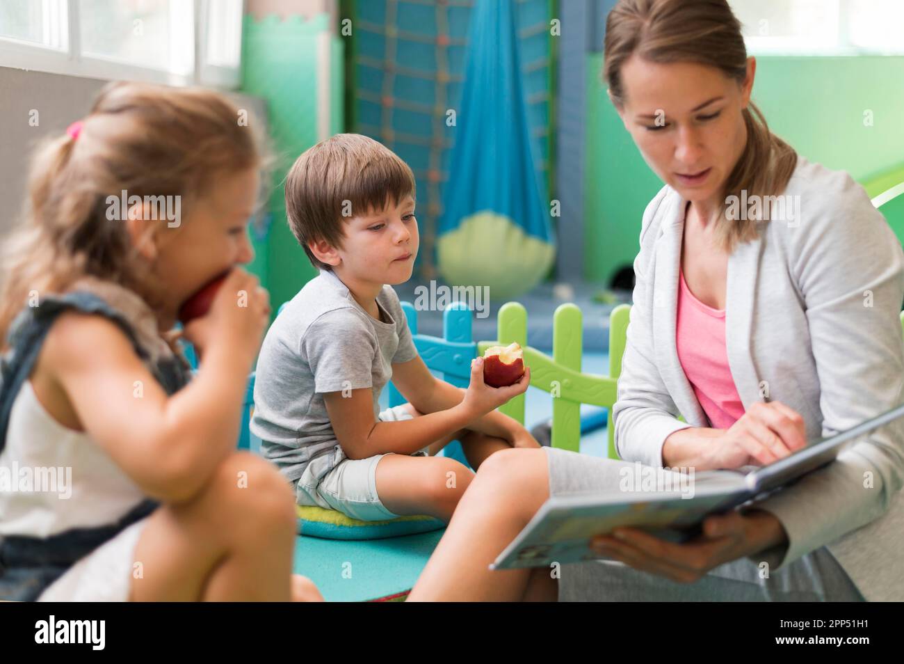 Medium shot teacher reading kids Stock Photo - Alamy