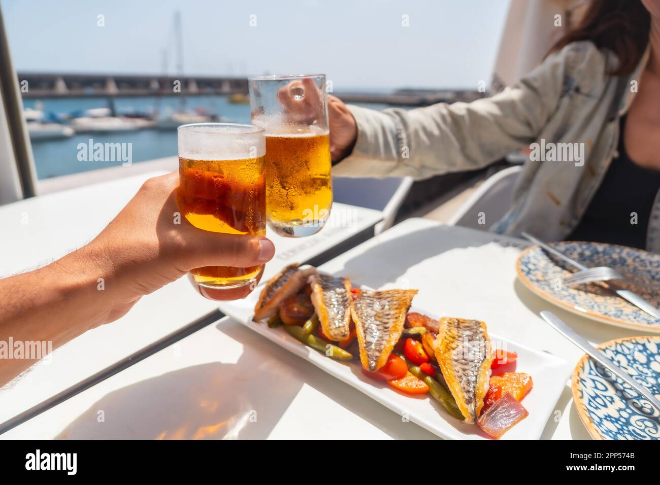 A couple toasting with beer by the sea eating fried fish, traditional ...