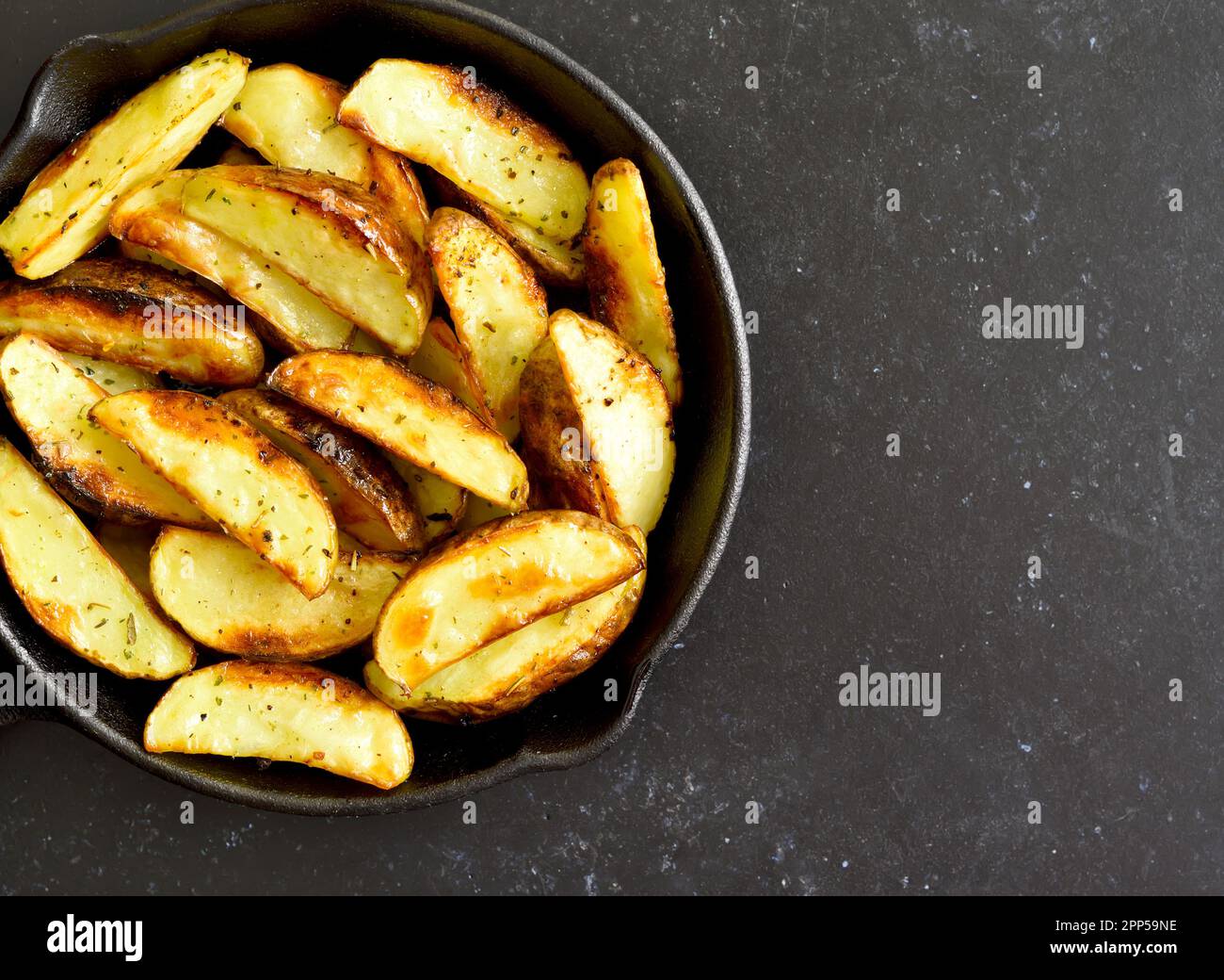 Potato wedges in frying pan over black background with copy space. Top ...