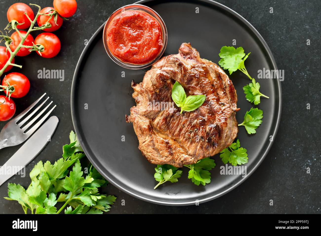 Fried beef steak and tomato sauce on plate over black stone table. Top ...