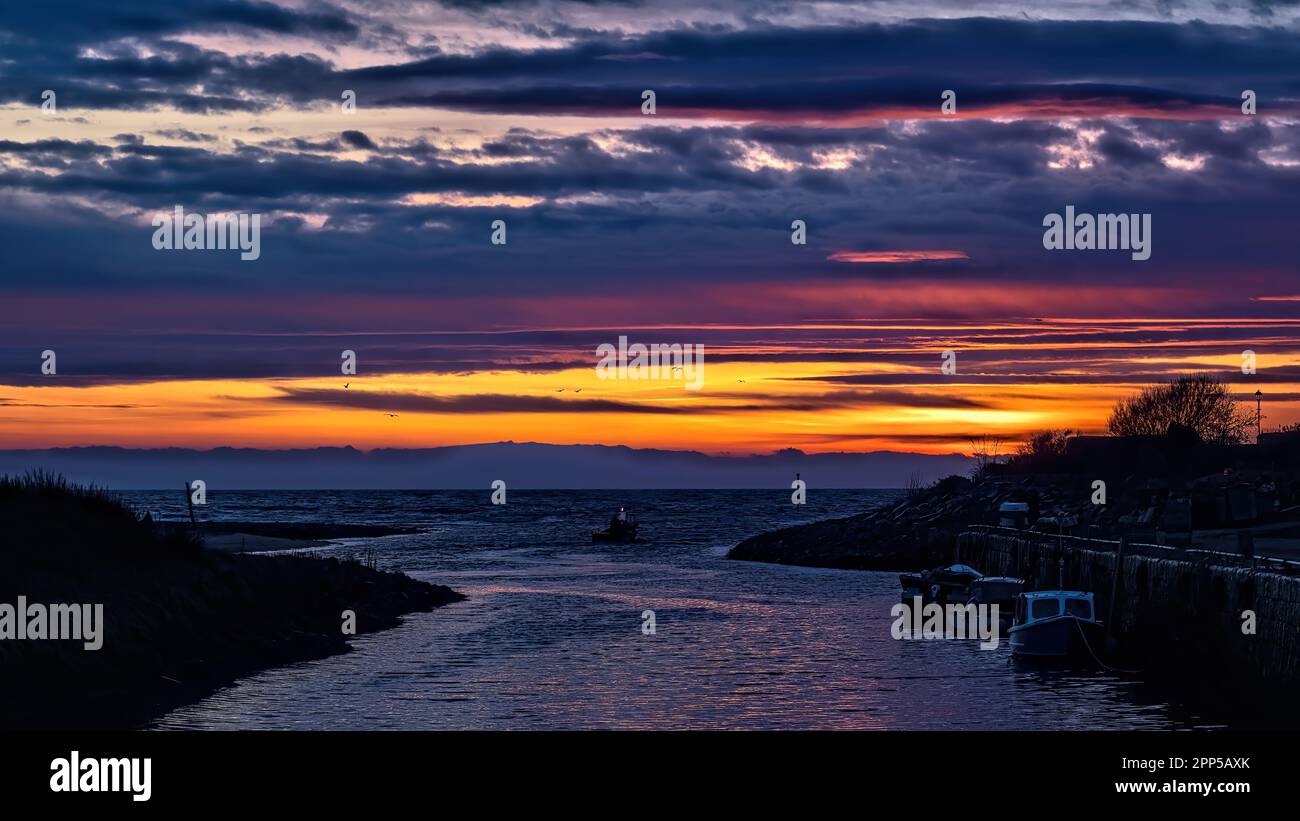 Boat sailing from Brora harbour at sunrise with dawn colours in the sky ...