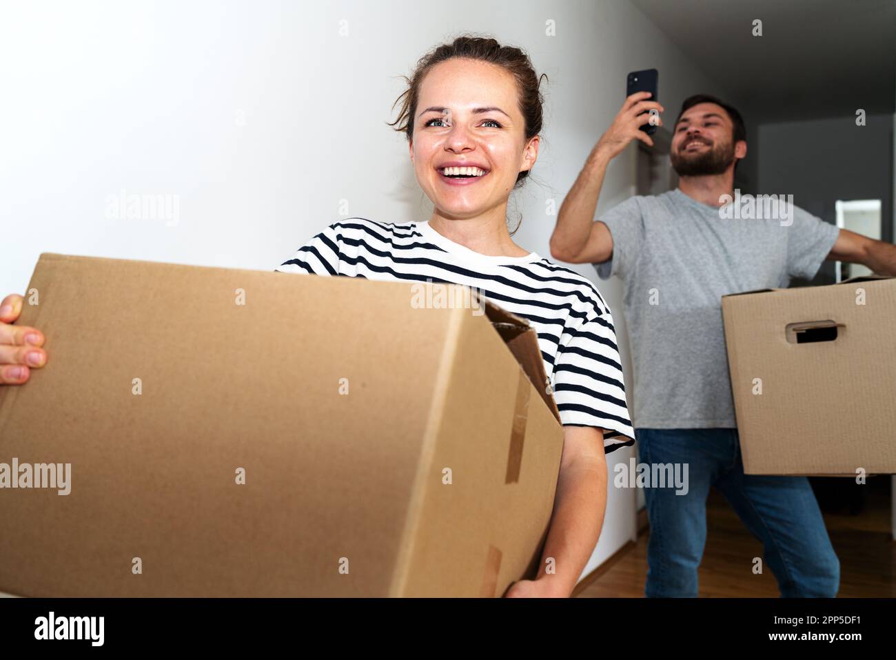 Happy married couple moving into their new apartment, carrying carton ...