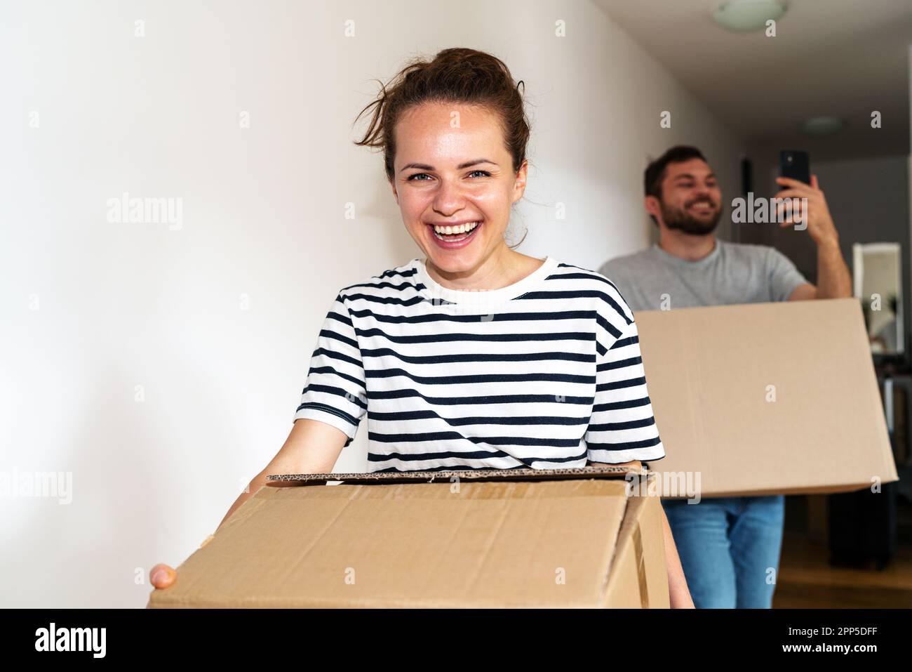 Happy young couple moving into a new apartment, carrying cardboard ...
