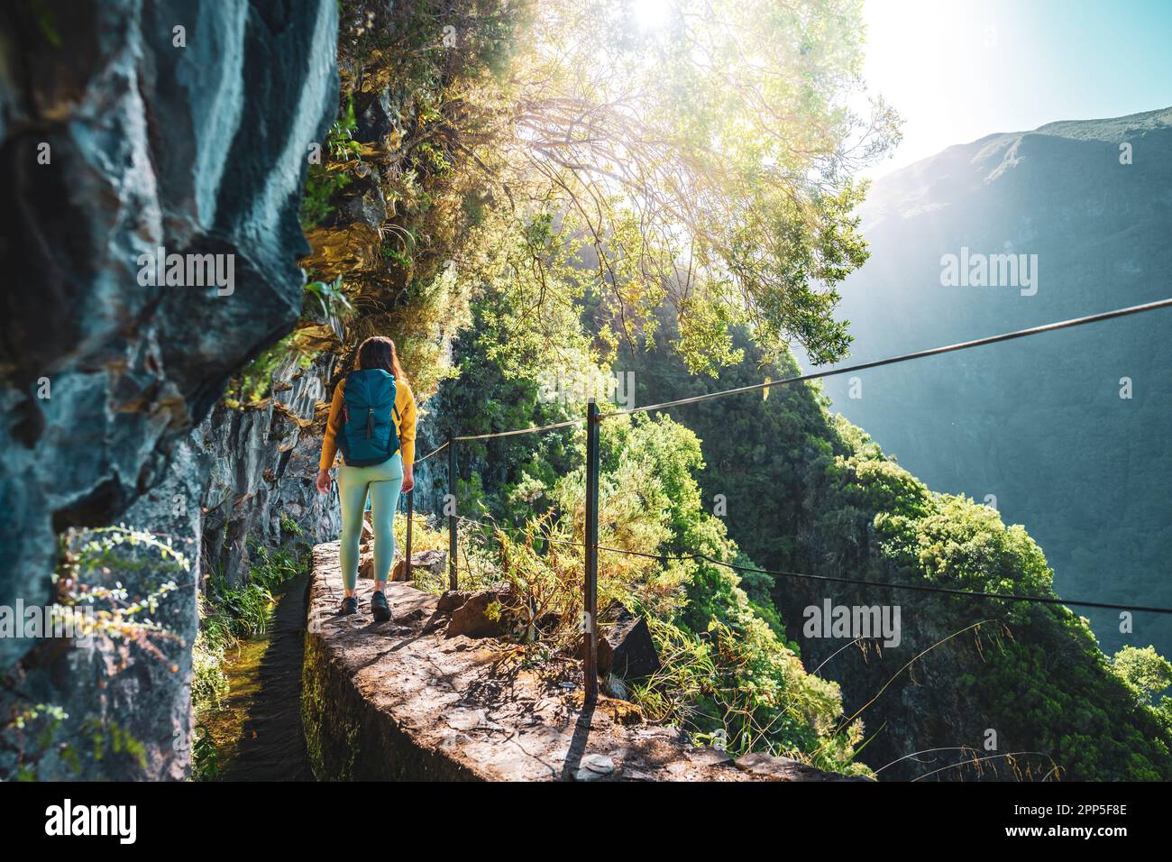 Description: Tourist woman walking below big rock wall along water ...