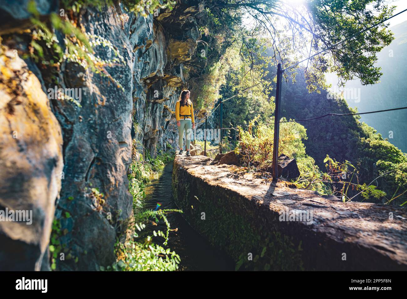 Description: Tourist woman walking below big rock wall along water ...