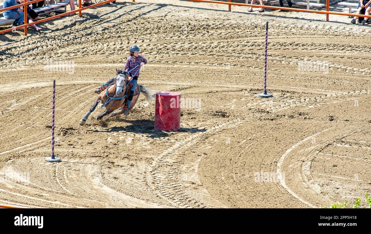 Teenage girl competing in an equine barrel competition in the summer ...