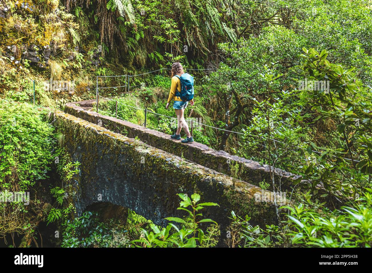 Description: Backpacker woman walking on overgrown footpath over old ...