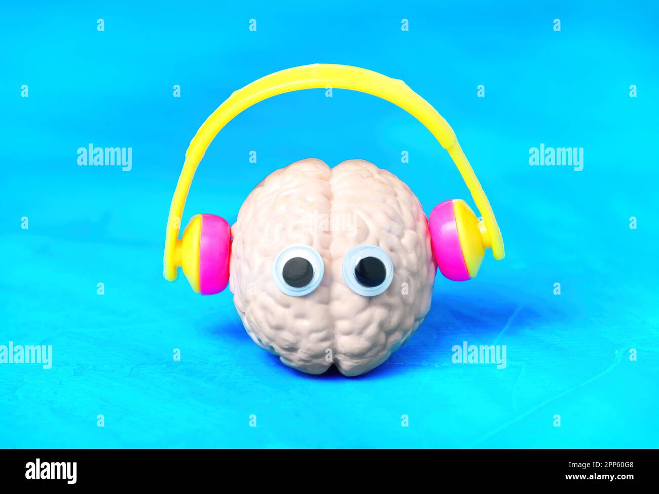 Toy human brain character with googly eyes wears vibrant headphones ...