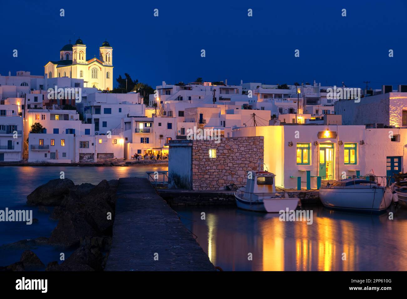Greek whitewashed houses and church by harbour watersfront after sunset ...