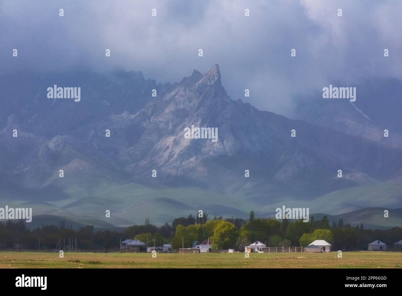 village at the foot of the mountains with rocky peaks in the clouds ...