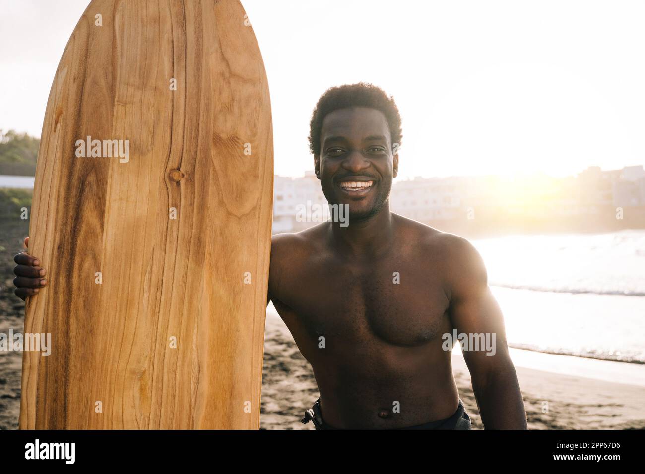 Happy African surfer holding surf wood surfboard after riding waves on ...